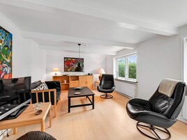 Uma sala de estar moderna com televisão de tela plana, poltronas de couro, mesa de centro de madeira e obras de arte nas paredes.