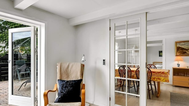 Quarto com uma cadeira de madeira, porta de vidro que dá para área externa e espaço de refeições com mesa e cadeiras.