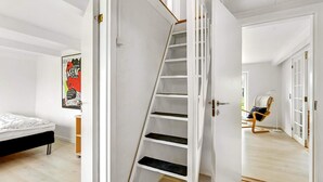 Quarto com cama branca, escada para um loft e um cartaz na parede.