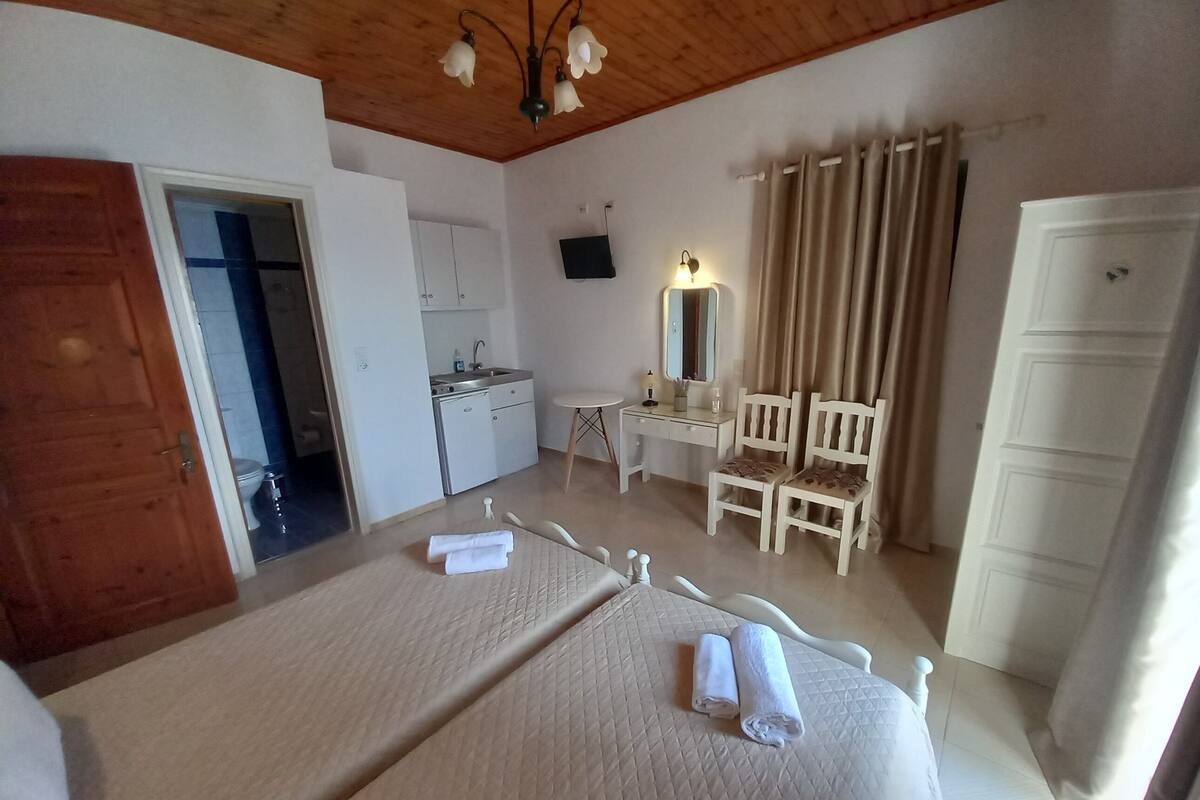 Quarto com cama, escrivaninha, cadeira, espelho, televisão e porta.