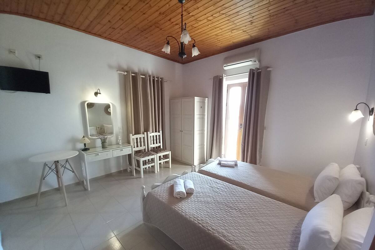 Quarto com duas camas, uma escrivaninha, uma cadeira, um espelho e um lustre.