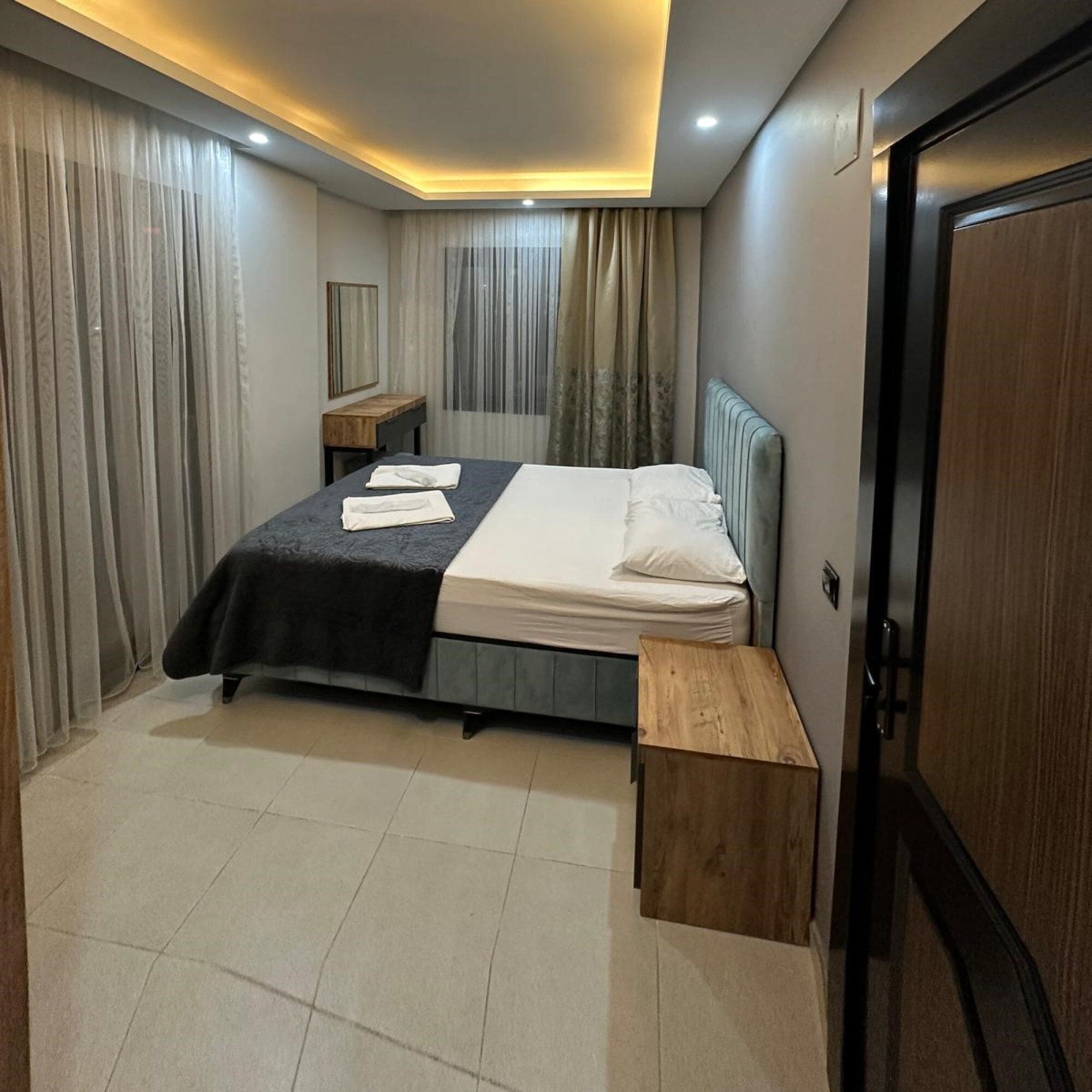 Um quarto moderno com uma cama, mesas de cabeceira, um banco de madeira e uma porta.