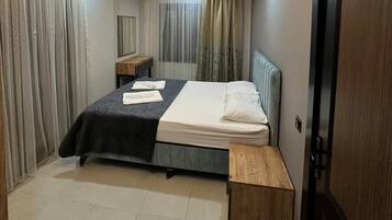 Um quarto moderno com uma cama, mesas de cabeceira, um banco de madeira e uma porta.