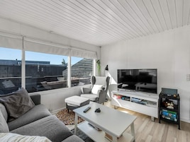 Uma sala de estar moderna com uma televisão grande, assentos confortáveis e vista para o exterior.