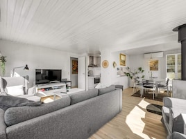 Uma sala de estar moderna com um sofá cinzento, televisão de tela plana e um espaço de refeições com mesa e cadeiras.