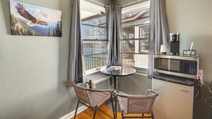 Quarto de canto com vista para montanhas, mesa de jantar, duas cadeiras de vime, micro-ondas e cafeteira.