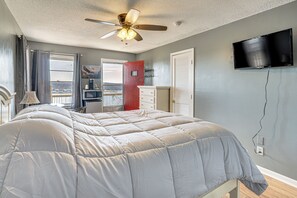 Quarto com cama, ventilador de teto, televisão na parede e janela com cortinas.