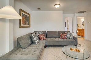 Uma sala de estar com um sofá modular cinza, uma mesa de centro de vidro e um quadro na parede.