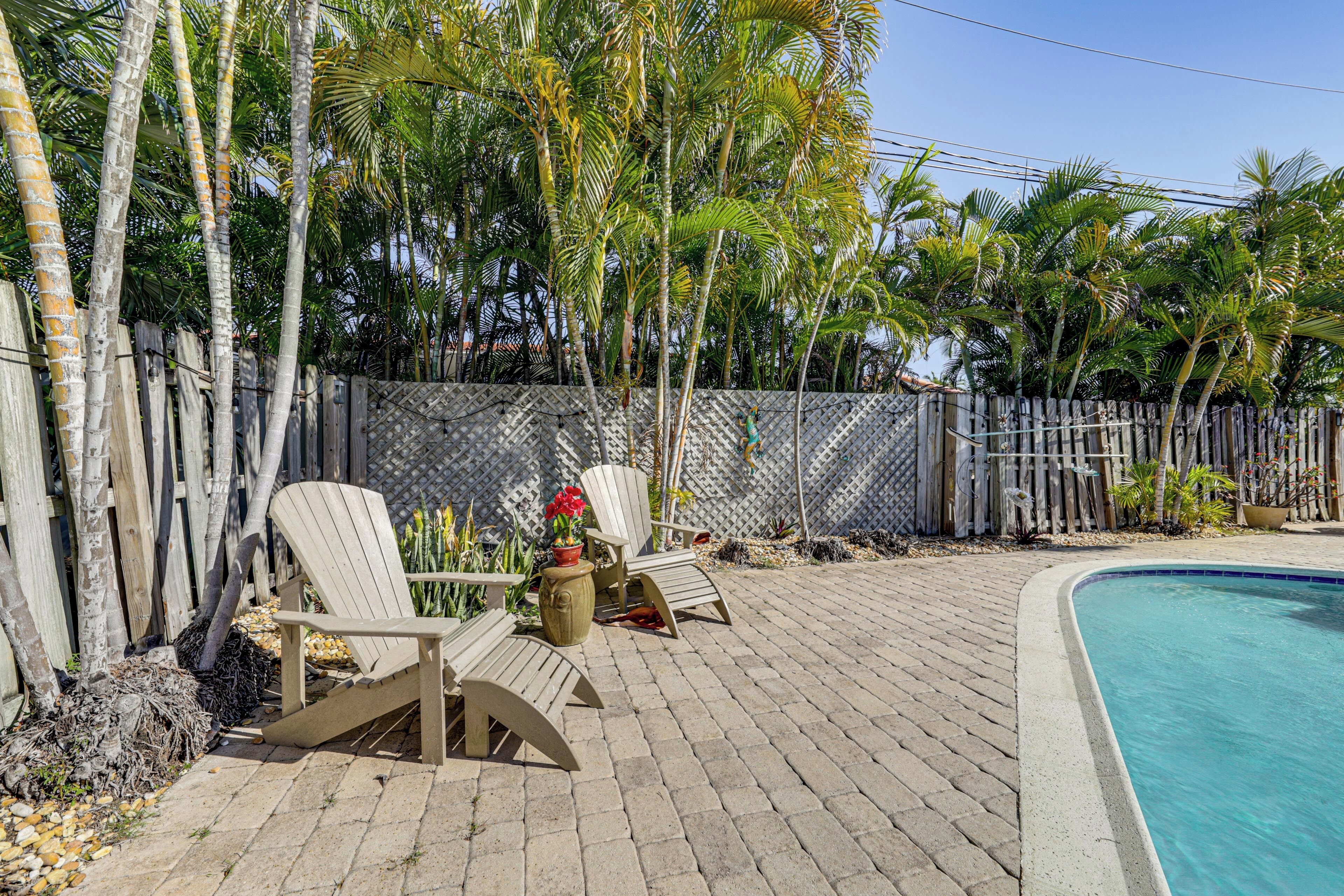 Área da piscina com cadeiras Adirondack, uma pequena mesa com um vaso de flores e um cercado de madeira.
