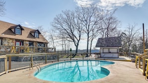 Uma piscina com design curvo, área de deck coberta e um edifício com telhado inclinado ao fundo.