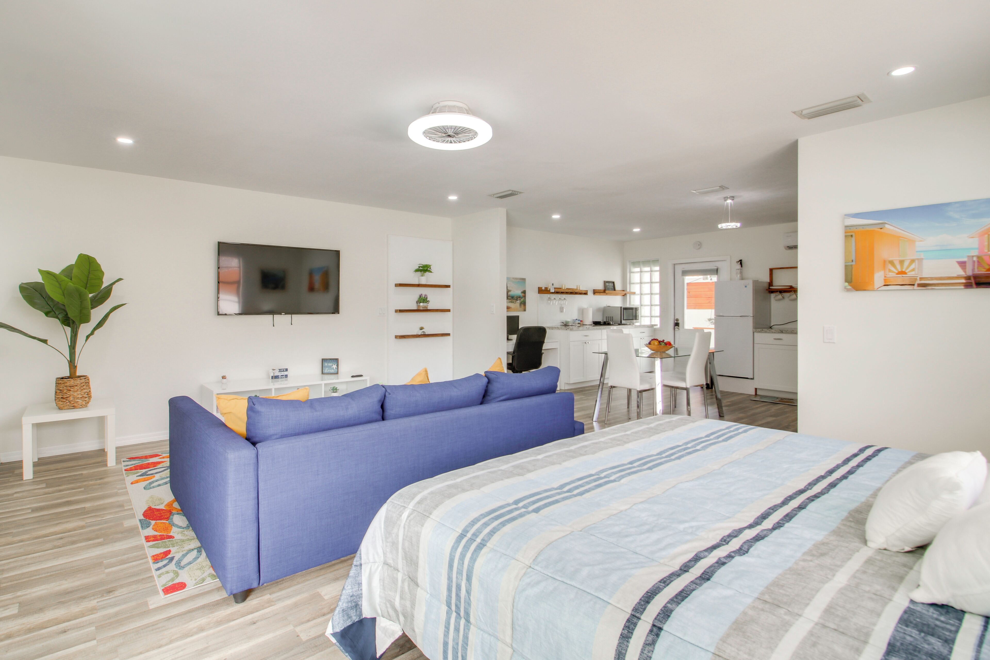 Uma sala de estar moderna com sofá, cama, televisão de tela plana, área de refeições e cozinha ao fundo.