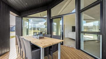 Interior moderno com deck de madeira, mesa de jantar com cadeiras e grandes janelas com vista para o exterior.
