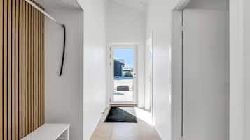 Corredor com parede de ripas de madeira, porta branca e vista para o exterior.