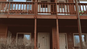 A two-story wooden building with a balcony, a front door, and a staircase leading to the entrance.