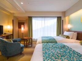 Quarto de hotel com duas camas, uma escrivaninha, uma cadeira e uma televisão.