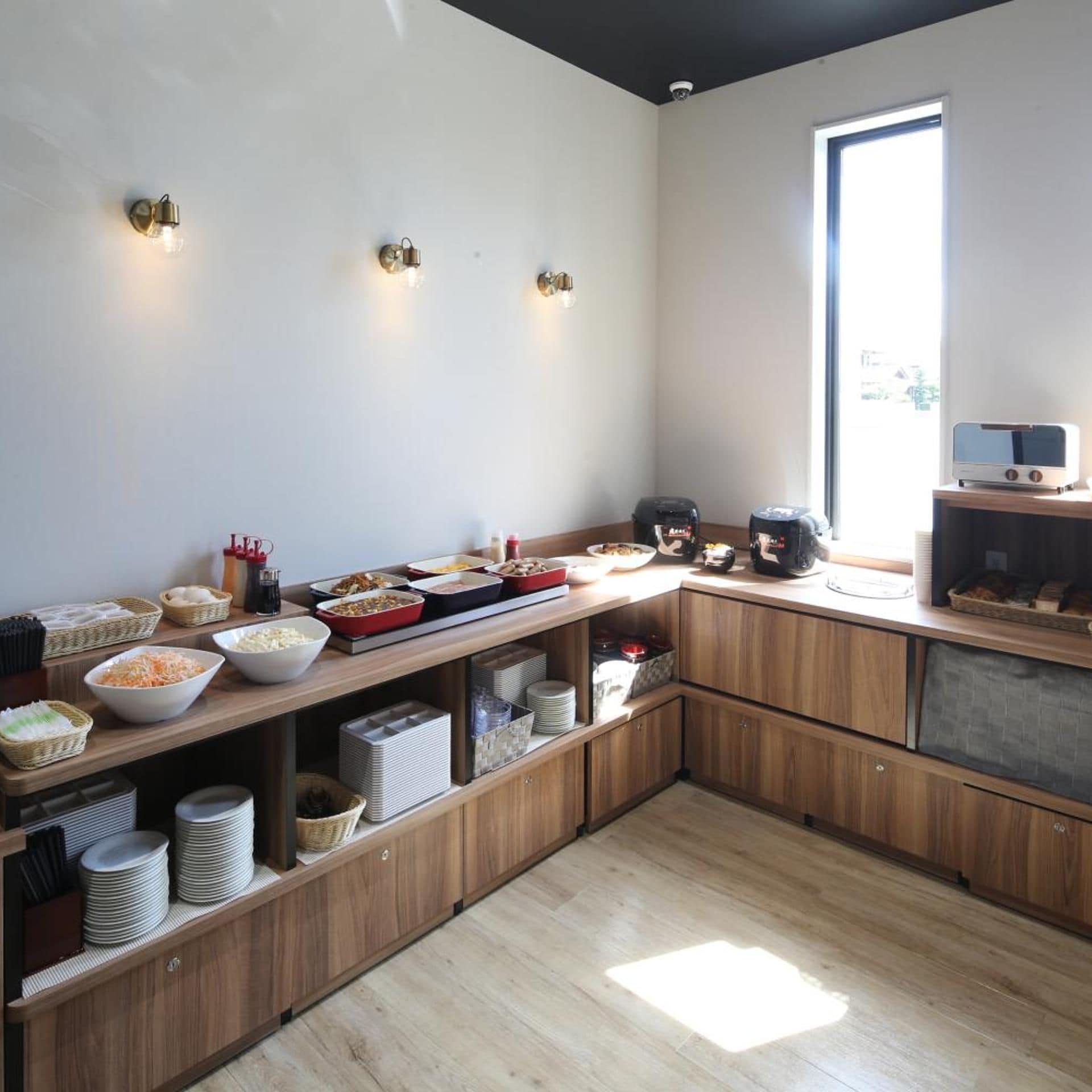 Cozinha com armários de madeira, mesa de buffet com comida e uma janela.
