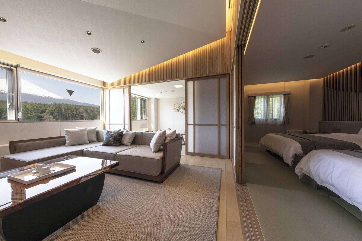Quarto de hotel moderno com sofá, cama, mesa de cabeceira e vista para uma montanha.