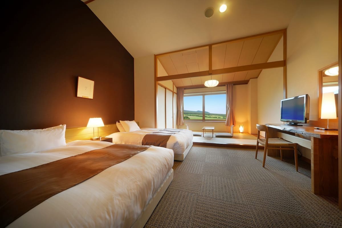 Quarto de hotel com duas camas, uma mesa de escritório com computador, uma cadeira e uma janela com vista.
