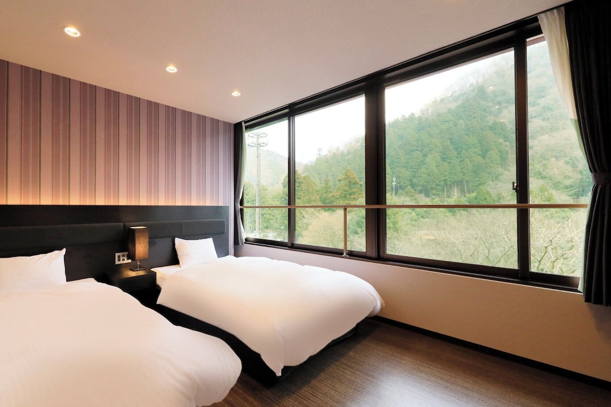 Quarto de hotel com duas camas, uma janela grande com vista para a floresta e uma parede listrada.