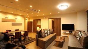 Uma sala de estar moderna com sofá, mesa de centro, televisão e um espaço de jantar com cadeiras e mesa.