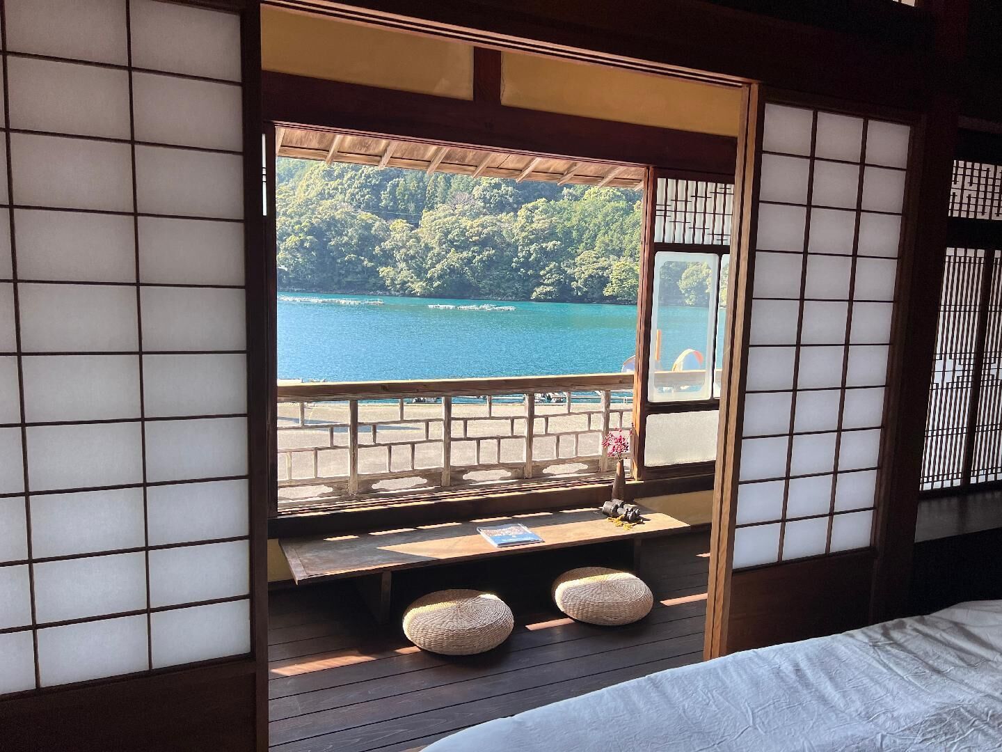 Um quarto japonês tradicional com tatames, um banco de madeira baixo e vista para um lago e uma floresta.