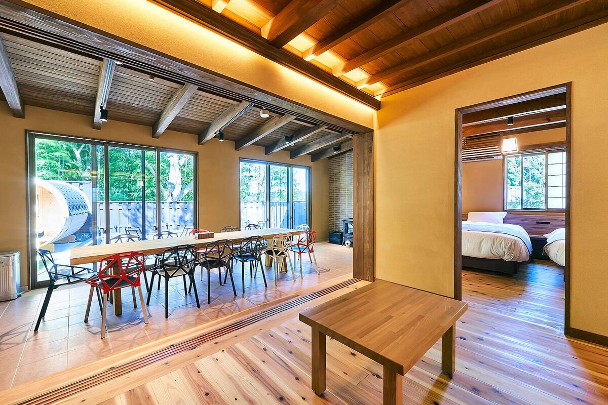 Um quarto espaçoso com uma longa mesa de madeira, várias cadeiras e uma cama no quarto adjacente.