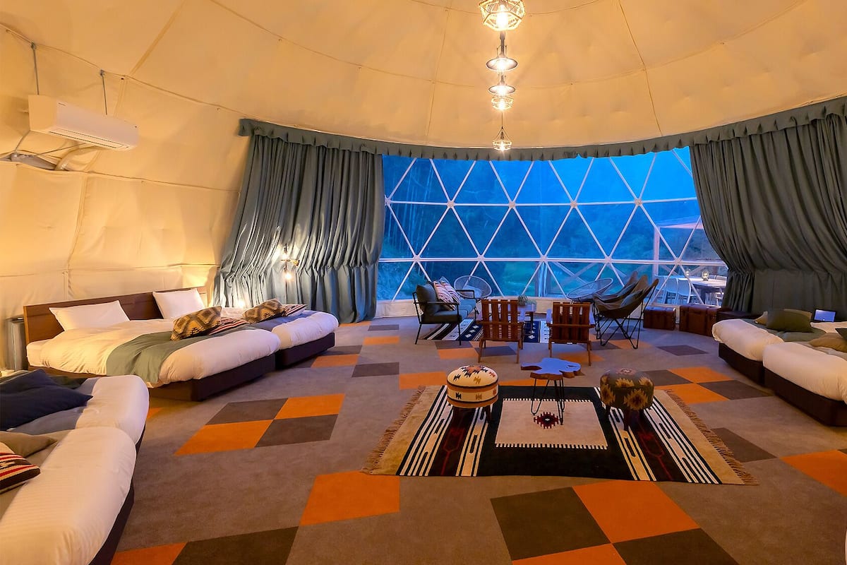 Um quarto amplo com uma grande janela, um sofá, uma poltrona e uma mesa de centro.