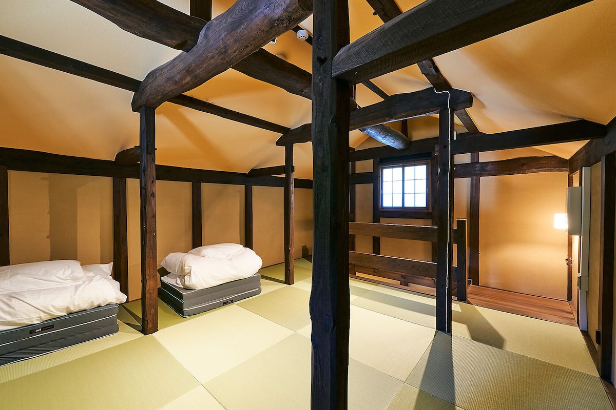 Quarto tradicional japonês com piso de tatame, vigas de madeira e teto baixo.
