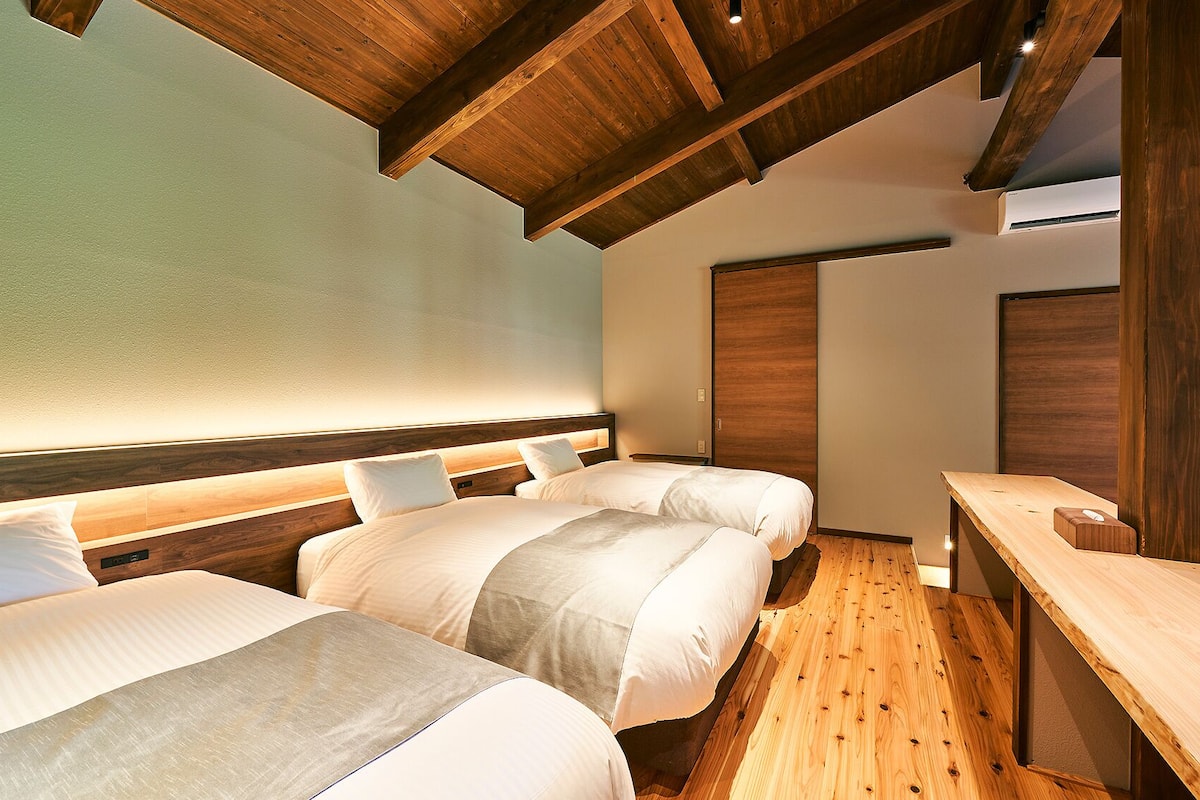Quarto de hotel com duas camas, vigas de madeira, uma mesa de madeira e um guarda-roupa.