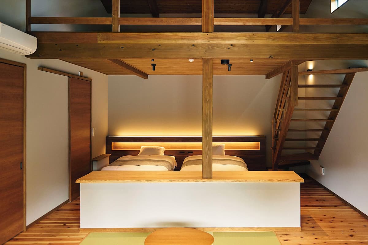 Quarto com teto em estilo loft, uma cama e escada de madeira.
