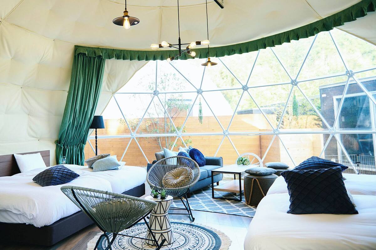 Um quarto em estilo tenda espaçoso, com uma cama, duas cadeiras, uma mesinha e uma janela grande.