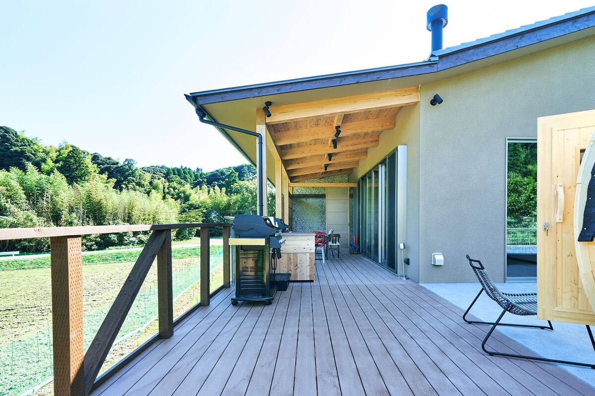 Um deck de madeira com churrasqueira, sauna e vista para uma área arborizada.