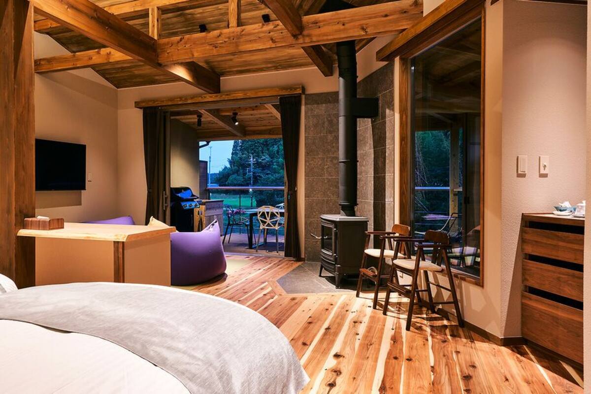 Quarto moderno com teto de madeira, cama, escrivaninha, cadeira e vista para o exterior.
