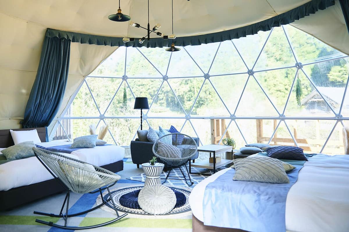 Um quarto estilo tenda acolhedor e bem iluminado, com uma janela grande, uma cama, uma cadeira e uma pequena mesa.