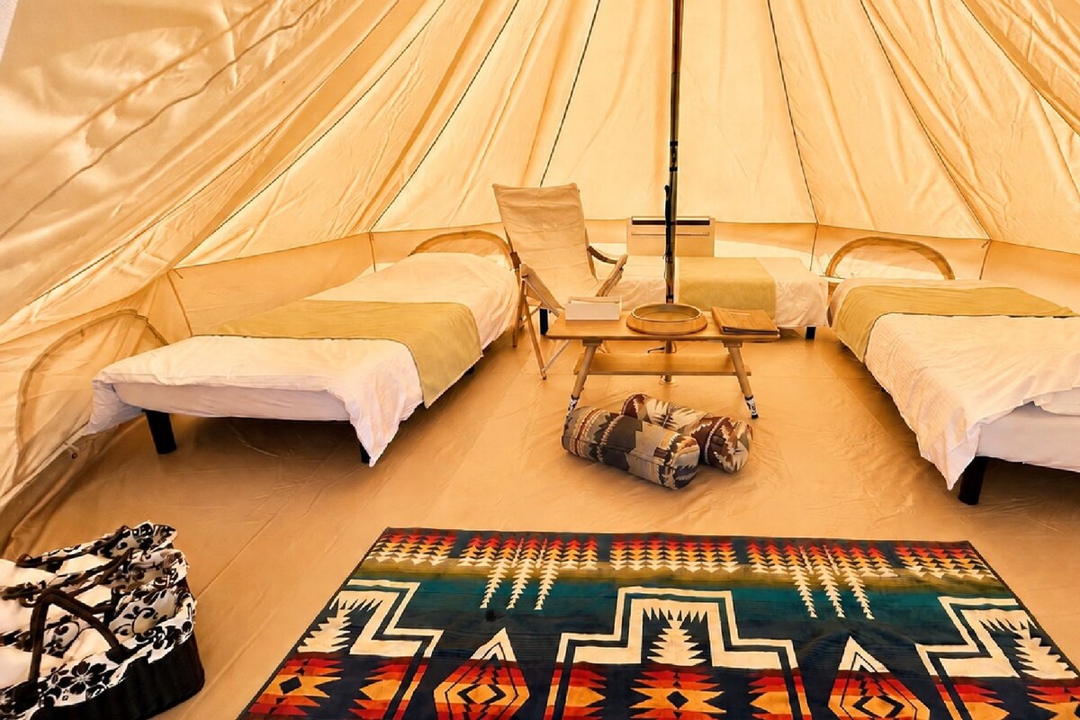 Uma tenda com duas camas, uma mesa e um tapete estampado.
