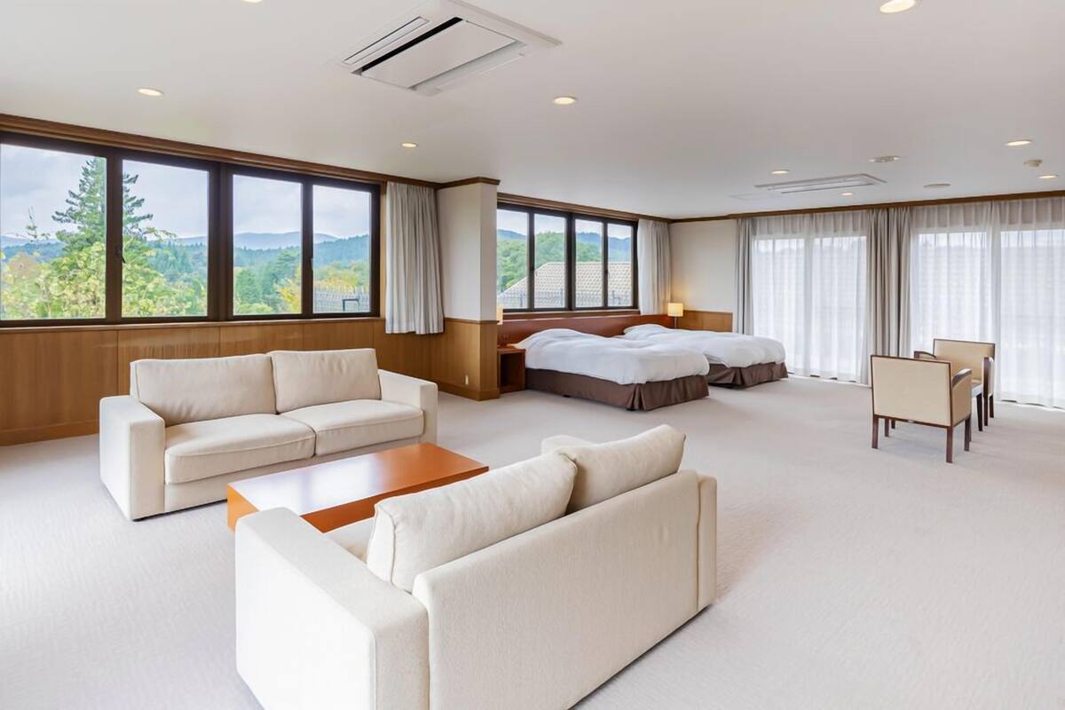 Quarto de hotel moderno com uma cama grande, um sofá, uma mesa de centro e uma escrivaninha com cadeiras.