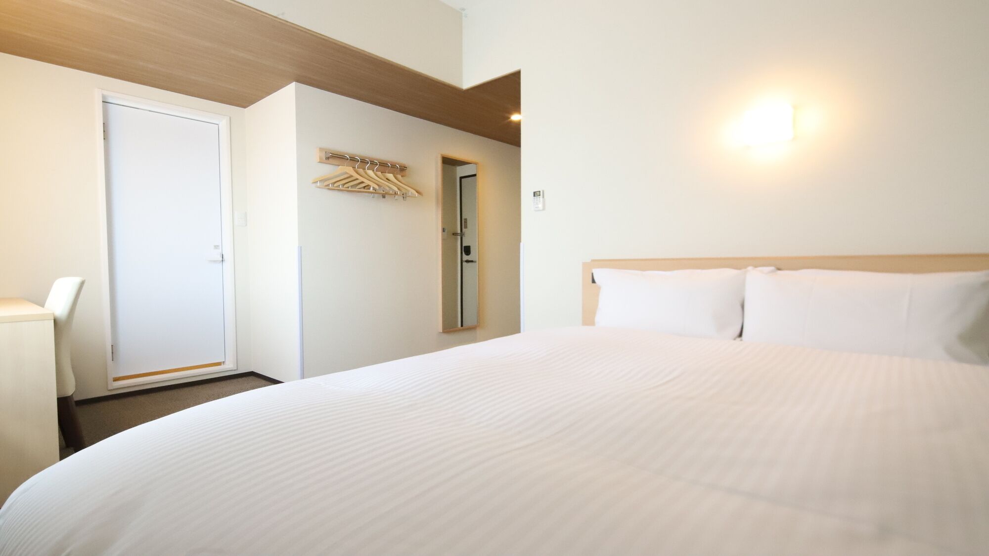 Quarto de hotel com cama, cadeira, cabideiro e porta.