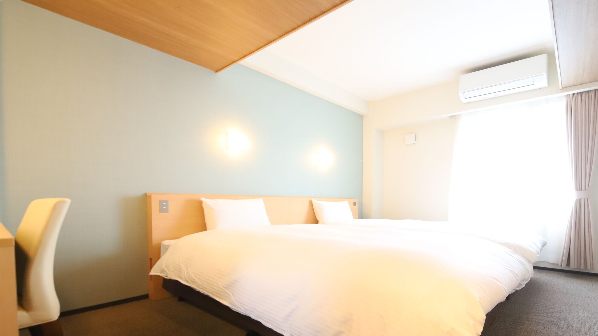 Quarto de hotel com cama, uma cadeira, uma luminária no teto e um aparelho de ar condicionado.