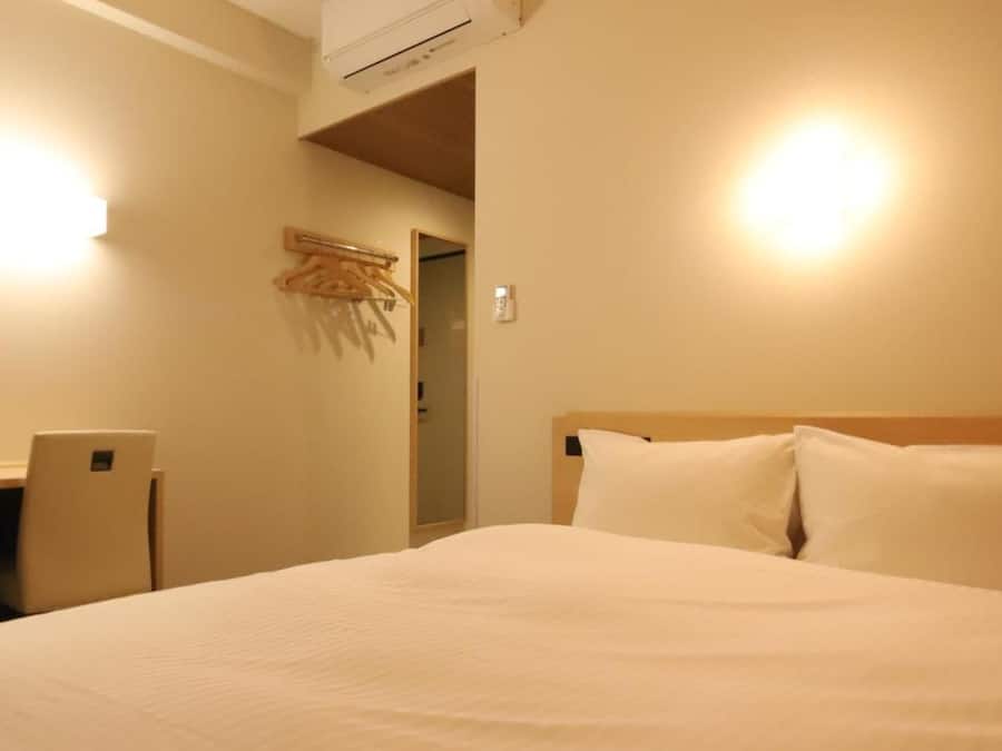Quarto de hotel com cama, escrivaninha e ar condicionado.