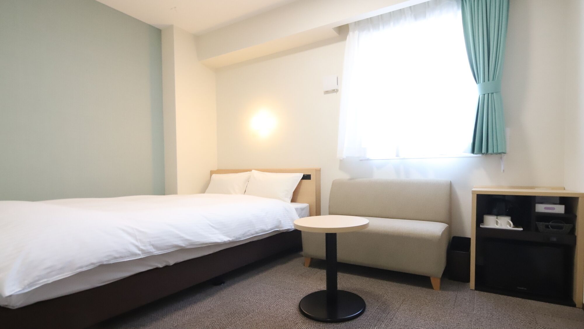 Quarto de hotel com cama, mesa redonda, sofá, pequeno armário e janela com cortinas.