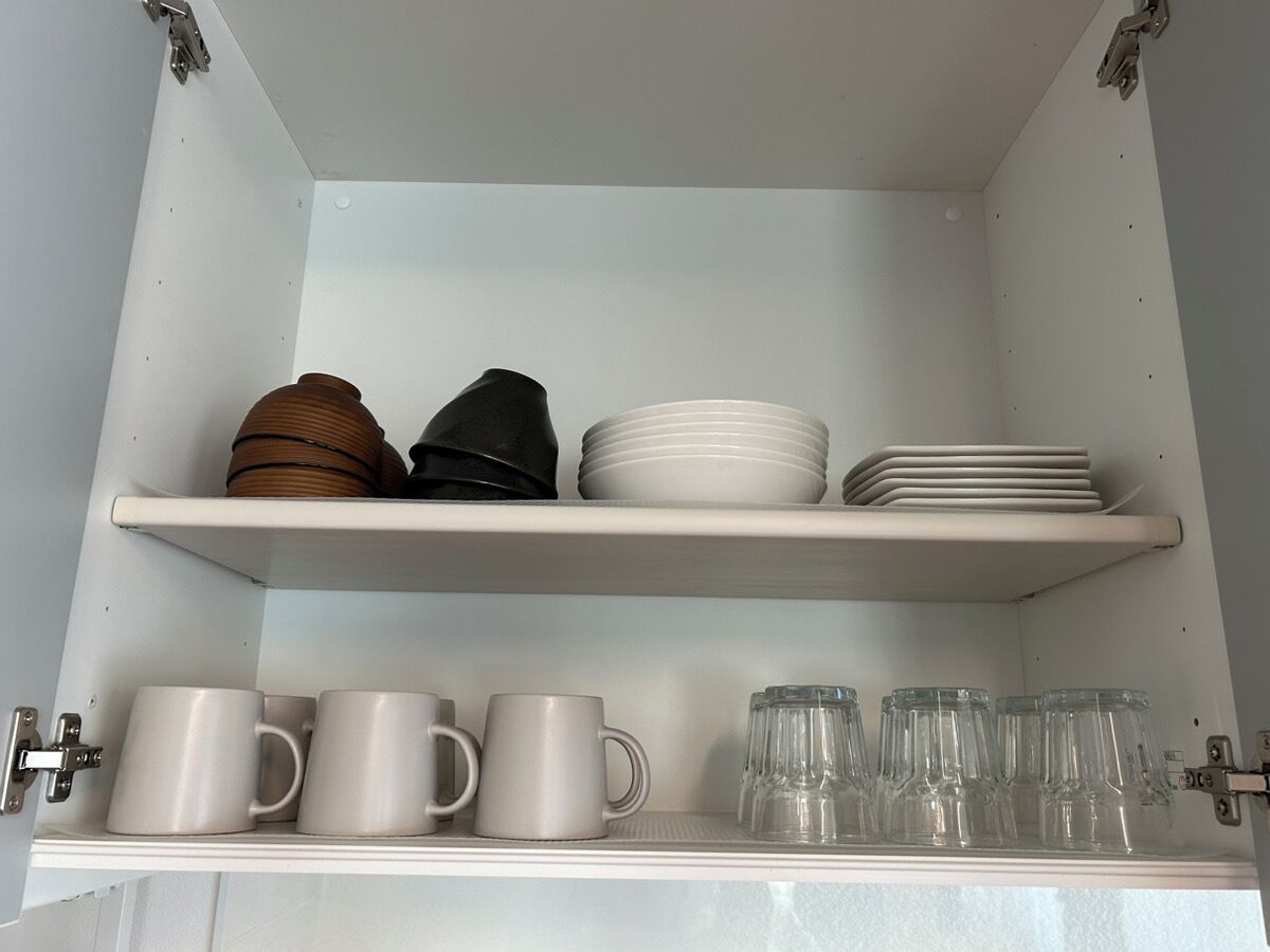 Um armário de cozinha com prateleiras contendo pratos, tigelas, canecas e copos.