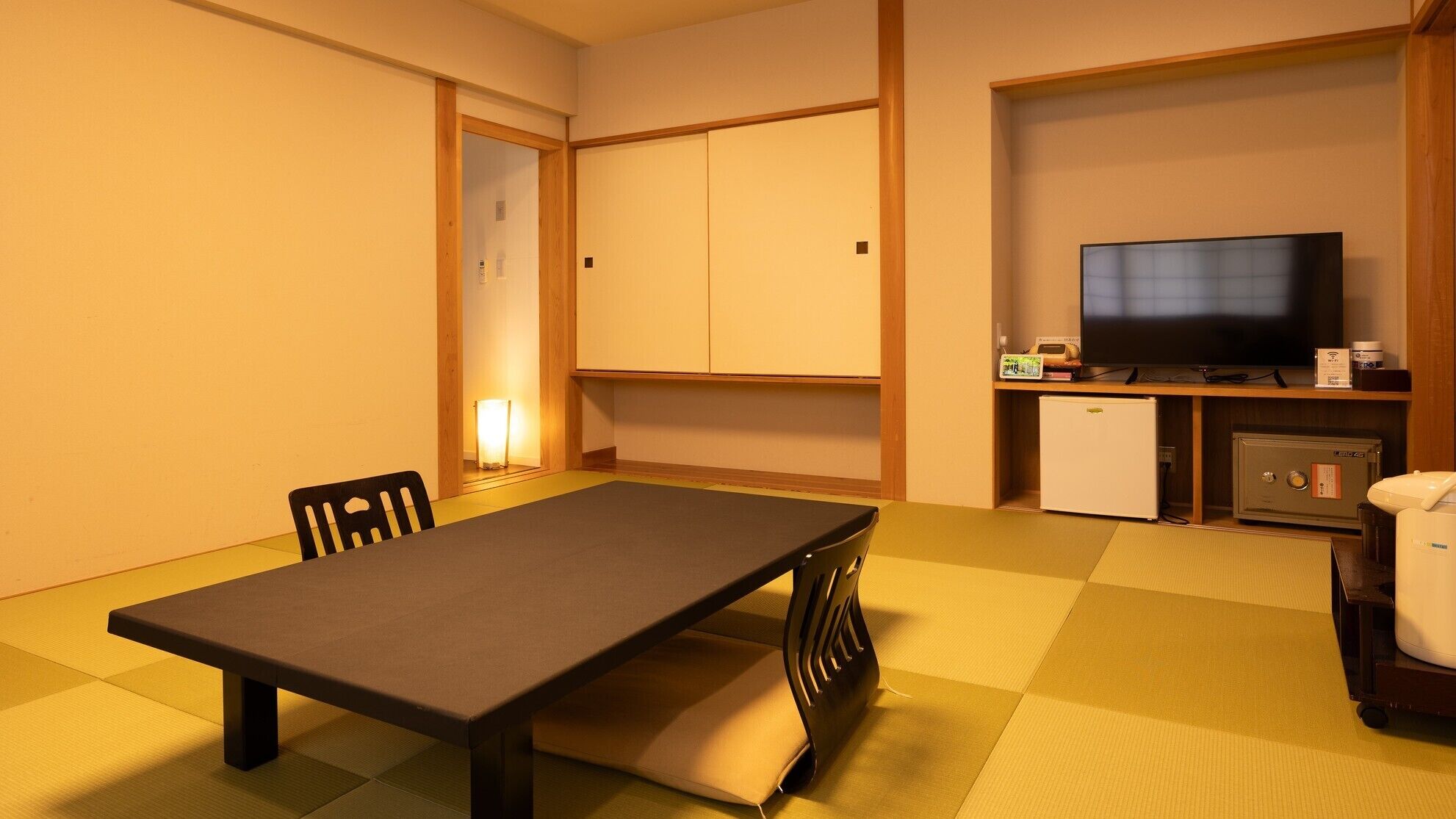 Quarto com tatames, mesa baixa, cadeiras, televisão, frigorífico e cofre.