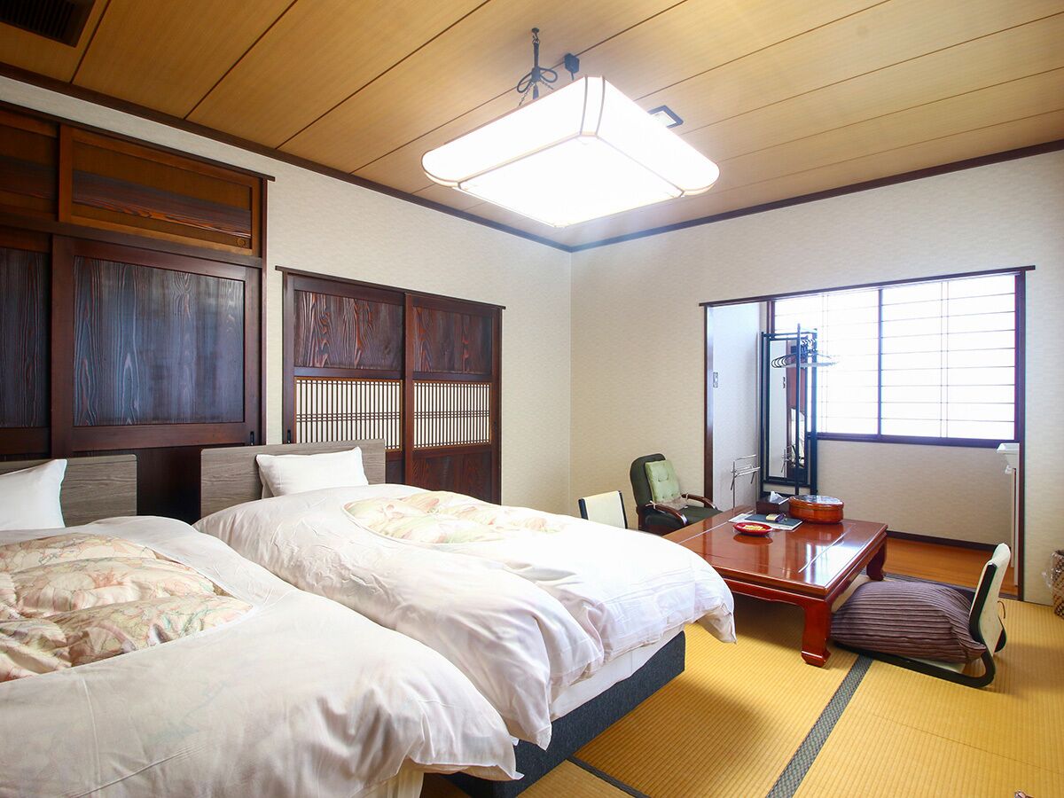 Quarto de hotel com duas camas, uma escrivaninha, uma cadeira, um espelho e uma janela.