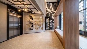 Interior moderno com elevador, design geométrico na parede e uma janela grande.