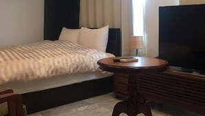 Quarto de hotel com uma cama, televisão, mesa pequena e janela com cortinas.
