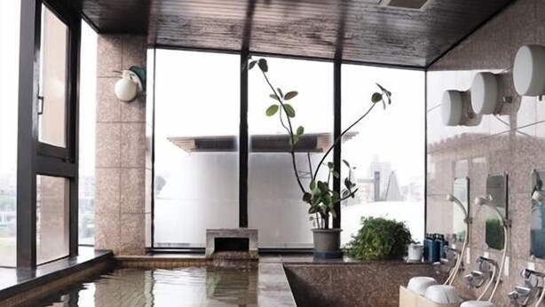 Piscina interior moderna com borda de pedra, área de estar com banquinhos brancos e vista para a cidade através de grandes janelas.