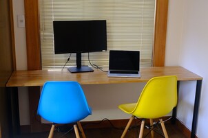 Um espaço de trabalho com uma escrivaninha, duas cadeiras, um monitor de computador e um laptop.