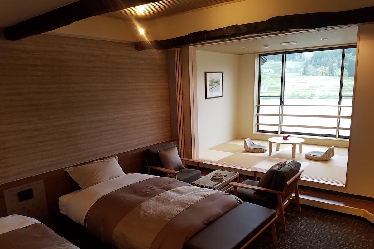 Quarto de hotel com cama, área de estar com mesa e uma grande janela com vista para o exterior.