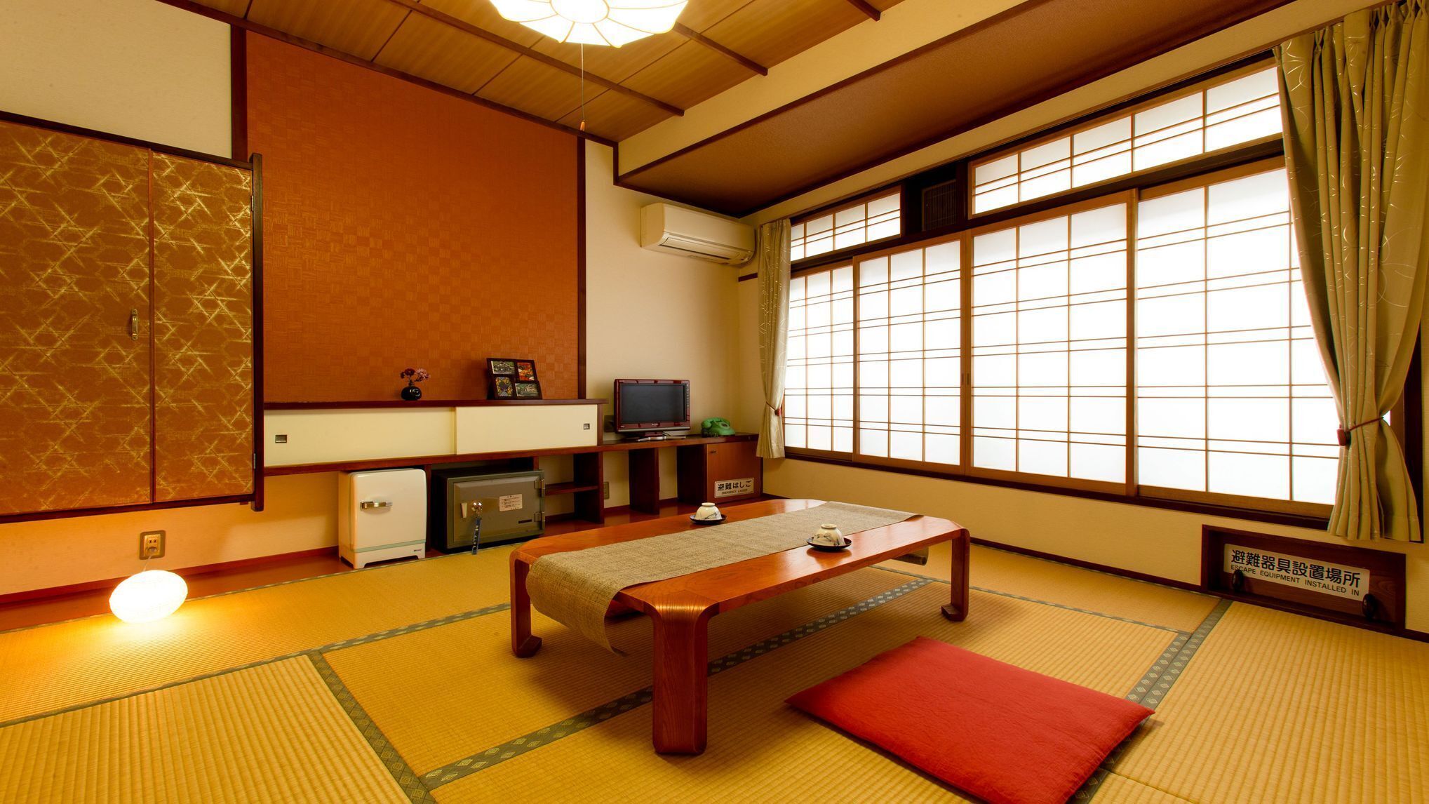 Um quarto japonês tradicional, com tatames, uma mesa de madeira baixa, uma televisão e uma cama futon.