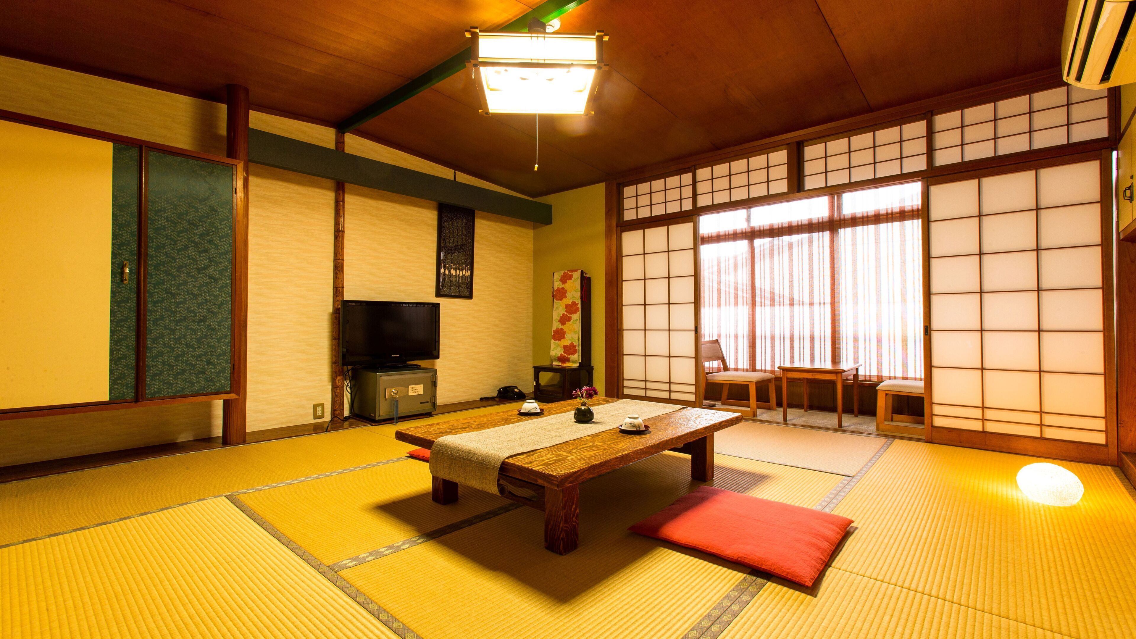 Um quarto japonês tradicional com tatames, uma mesa baixa, uma televisão e portas de correr.
